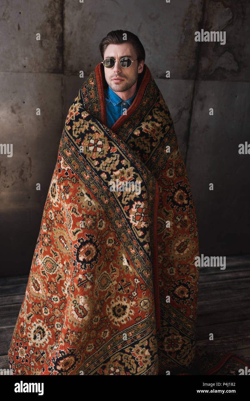 stylish young man covered in rug in front of concrete wall Stock Photo ...