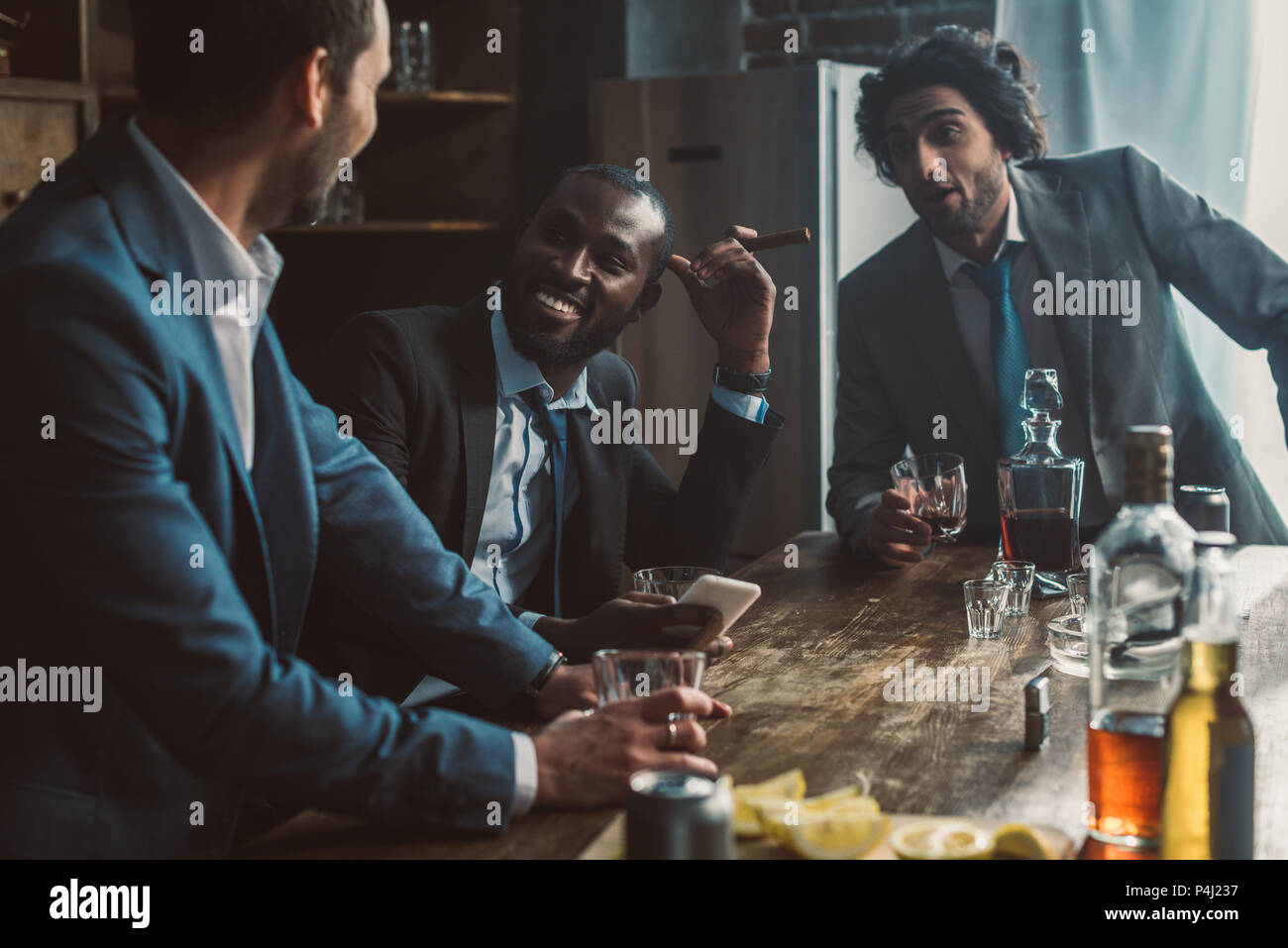 smiling multiethnic men talking, drinking whiskey and smoking cigars ...