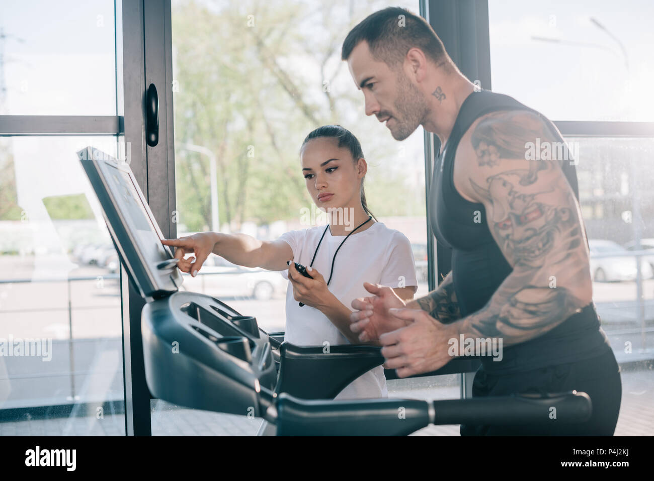 female personal trainer pointing at treadmill screen and running ...