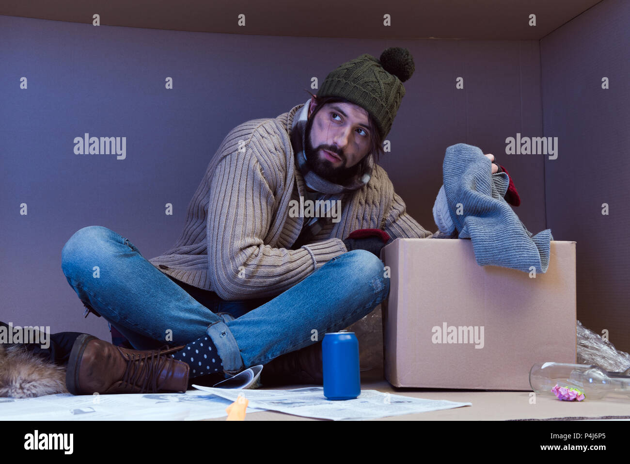 homeless man sitting in cardboard box with clothes Stock Photo - Alamy