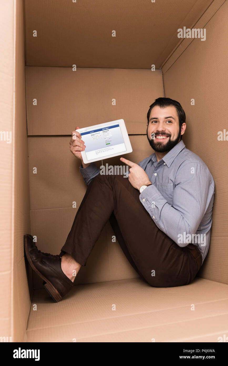 cheerful handsome man pointing at tablet with facebook website while ...