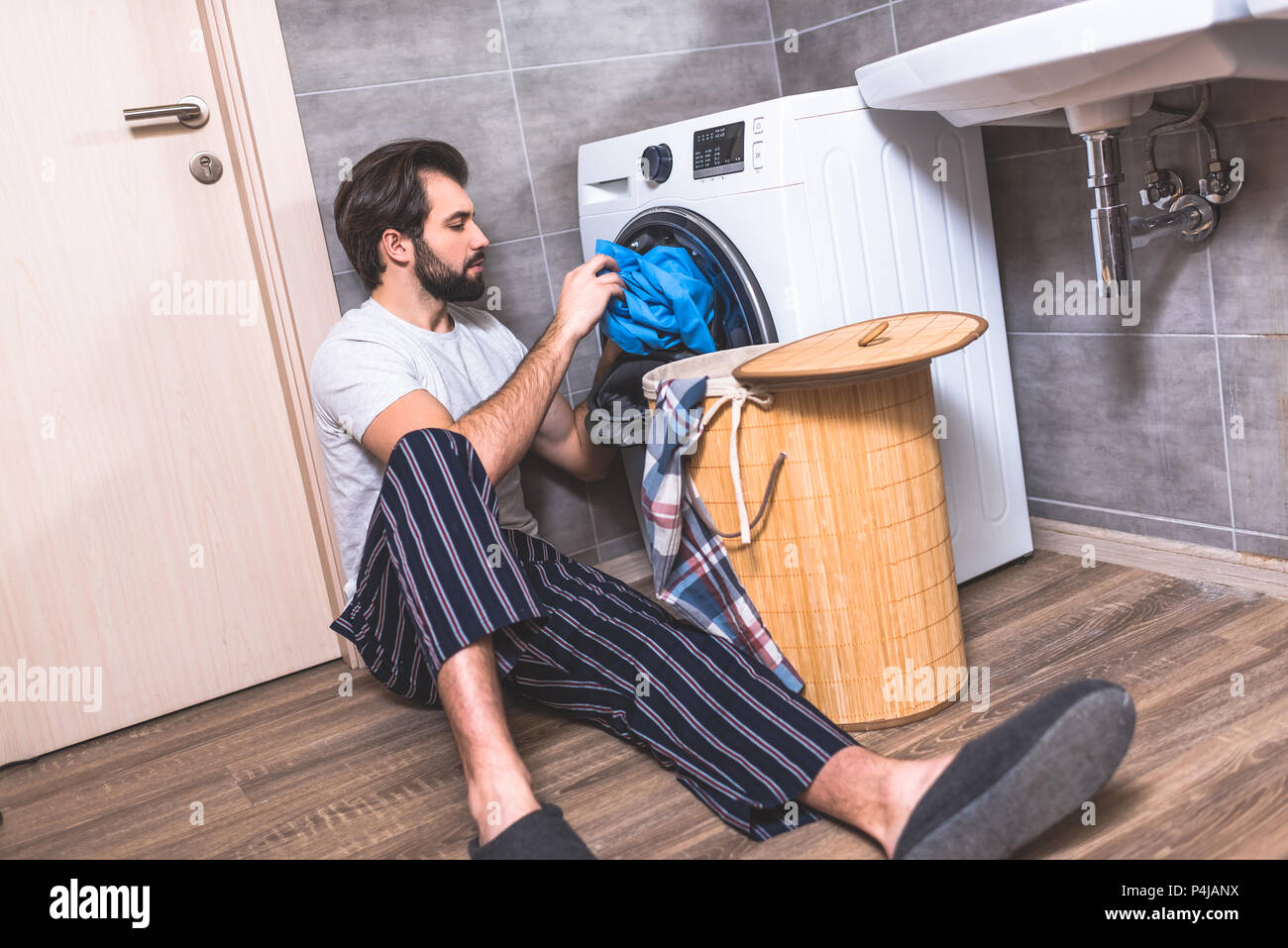 handsome loner putting laundry in washing machine in bathroom Stock ...