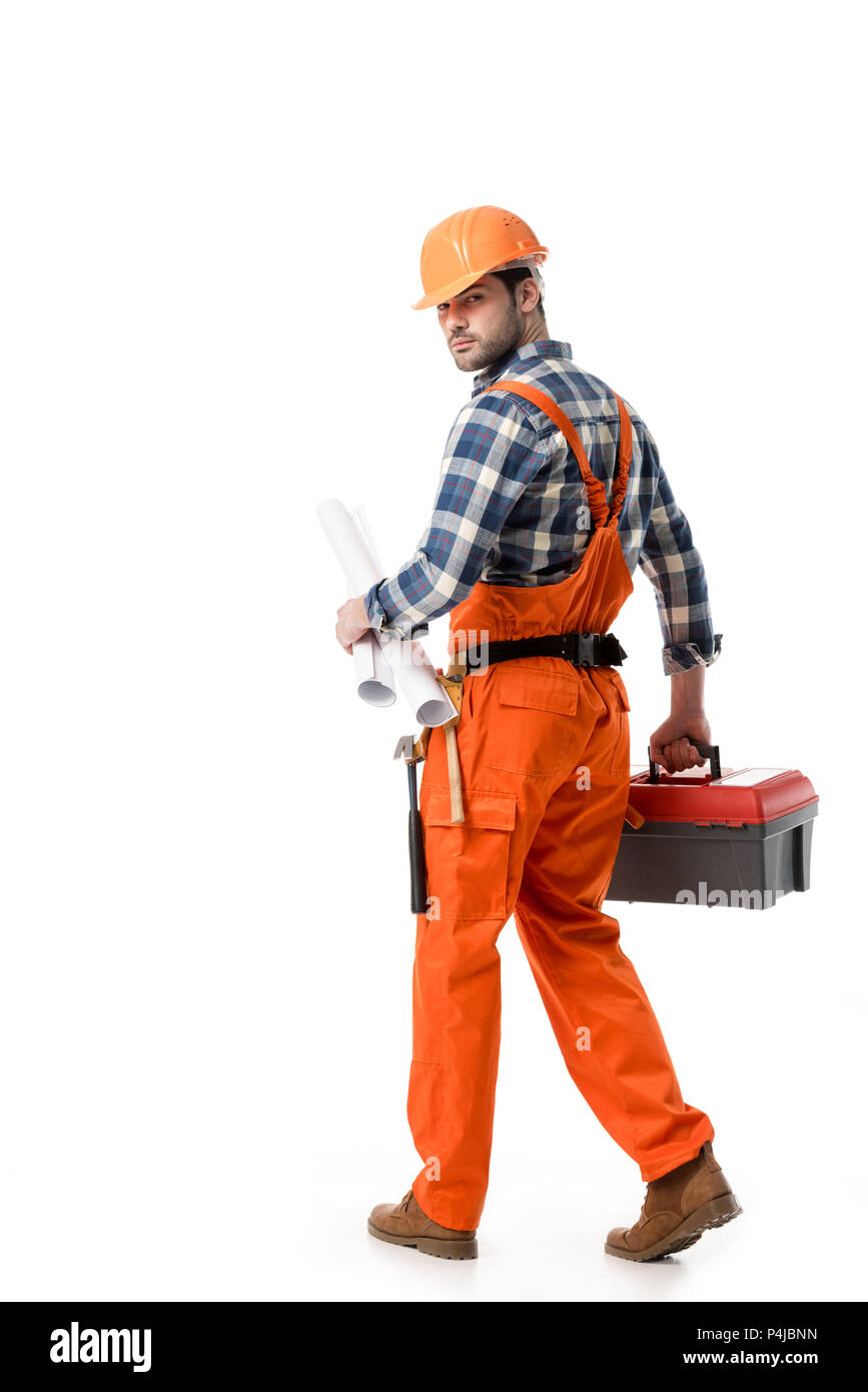 Young builder in orange overall and helmet carrying tool box and ...