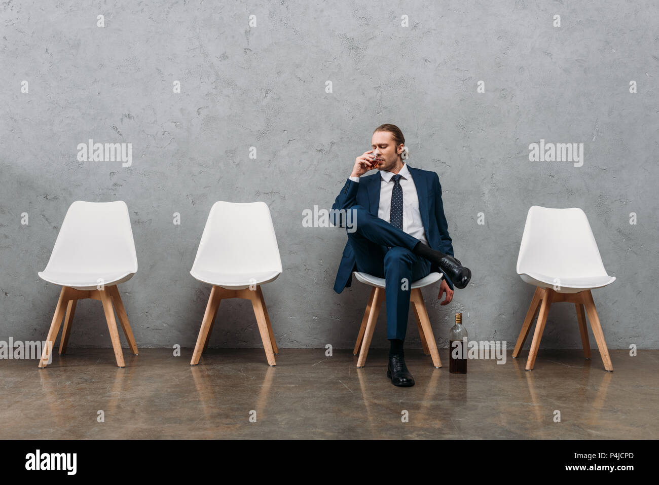 businessman drinking alcohol while sitting on chair under concrete wall ...