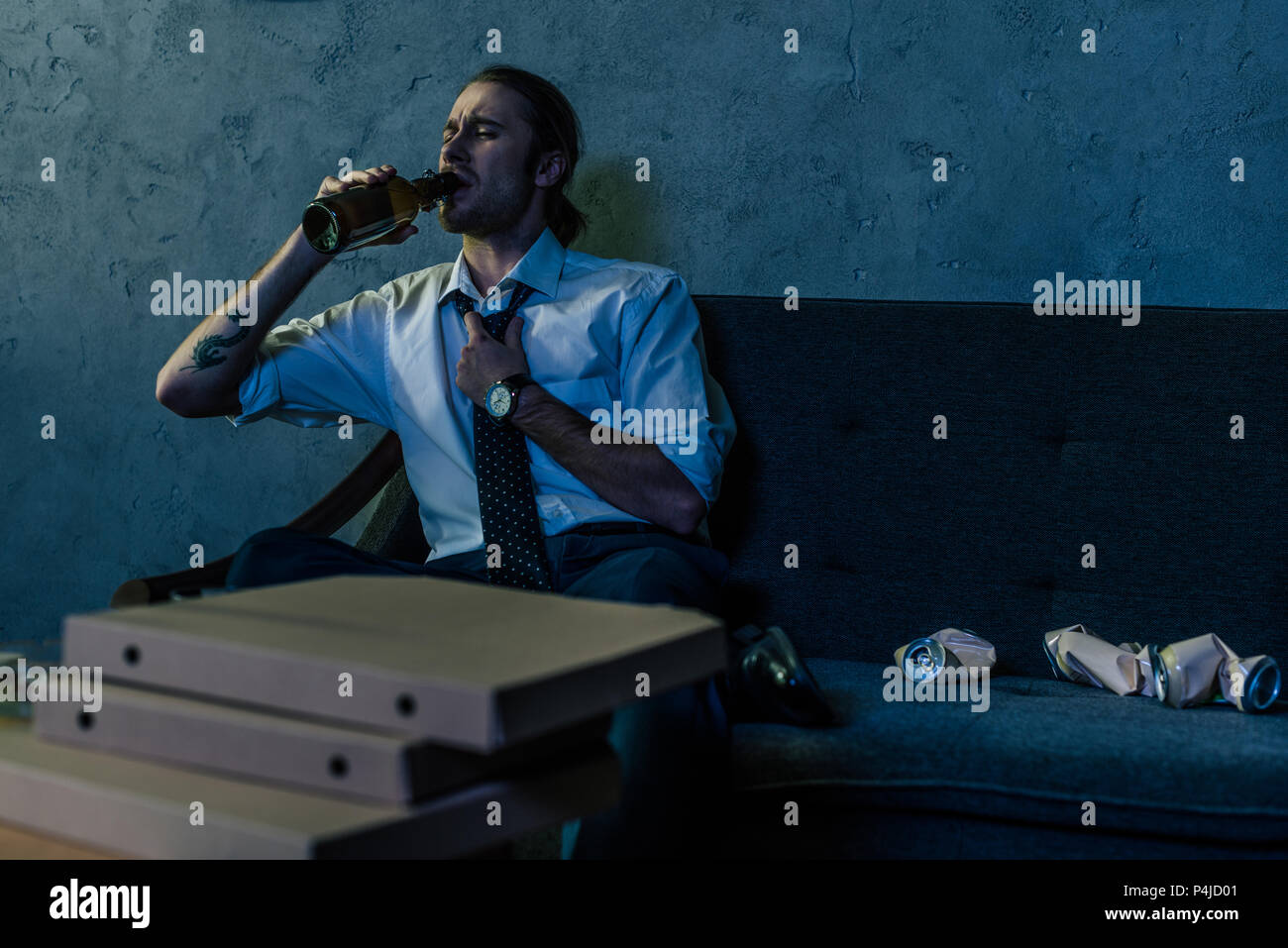 young alcohol addicted man drinking beer with pizza on couch after work ...