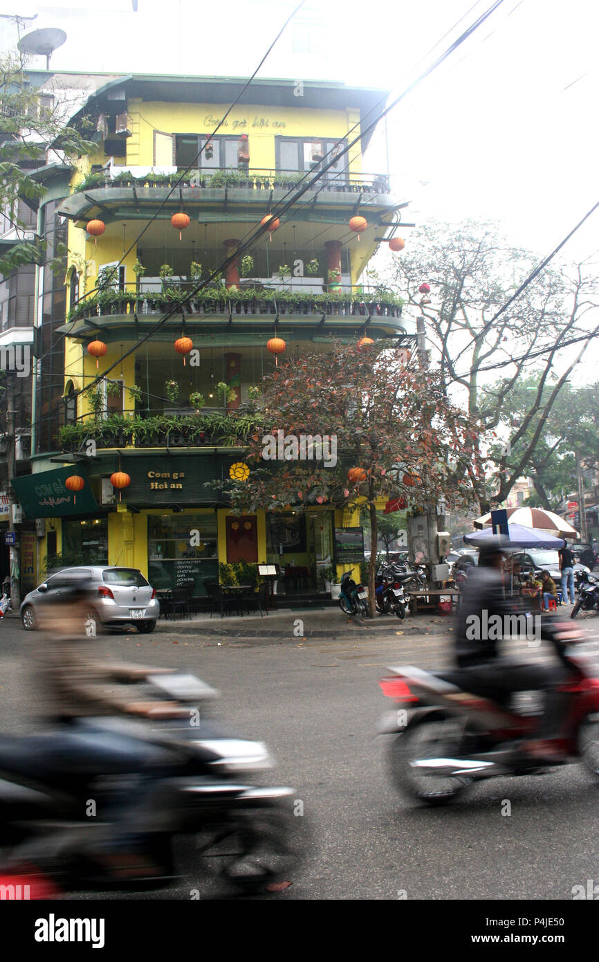 Blurred Mopeds passing Yellow and Green Building with Orange Lanterns ...