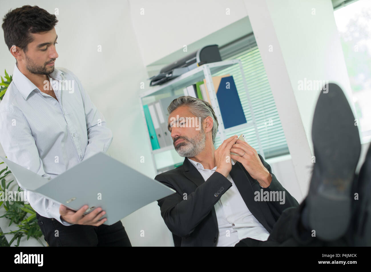 Assistant showing file to manager who has his feet on the desk Stock ...