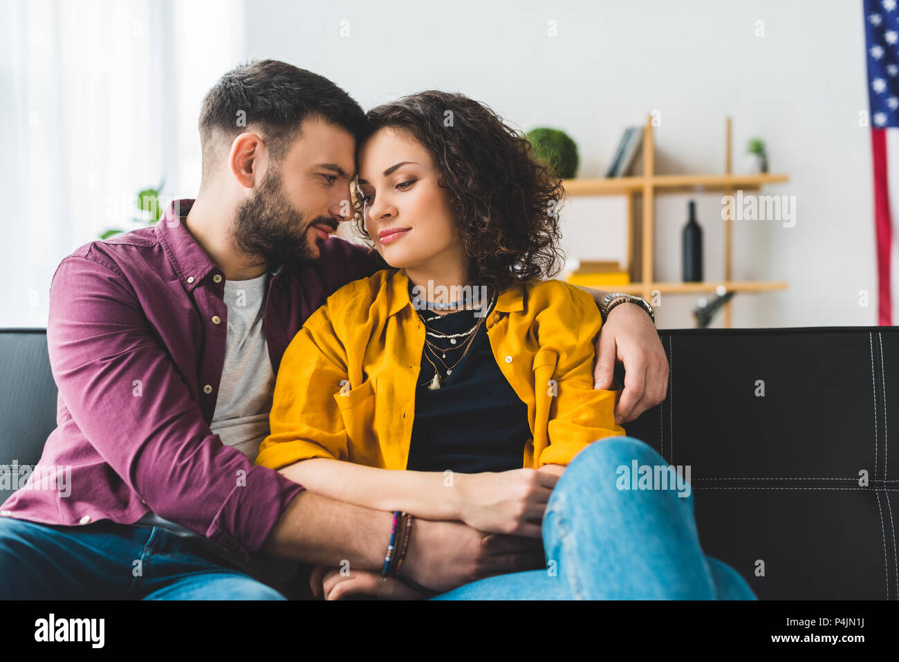 Close up of young man hugging his girlfriend while sitting on sofa ...