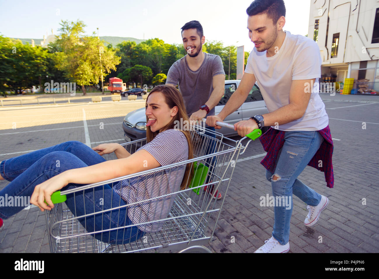 Two laughing young friends pushing their friend down a walkway in the ...