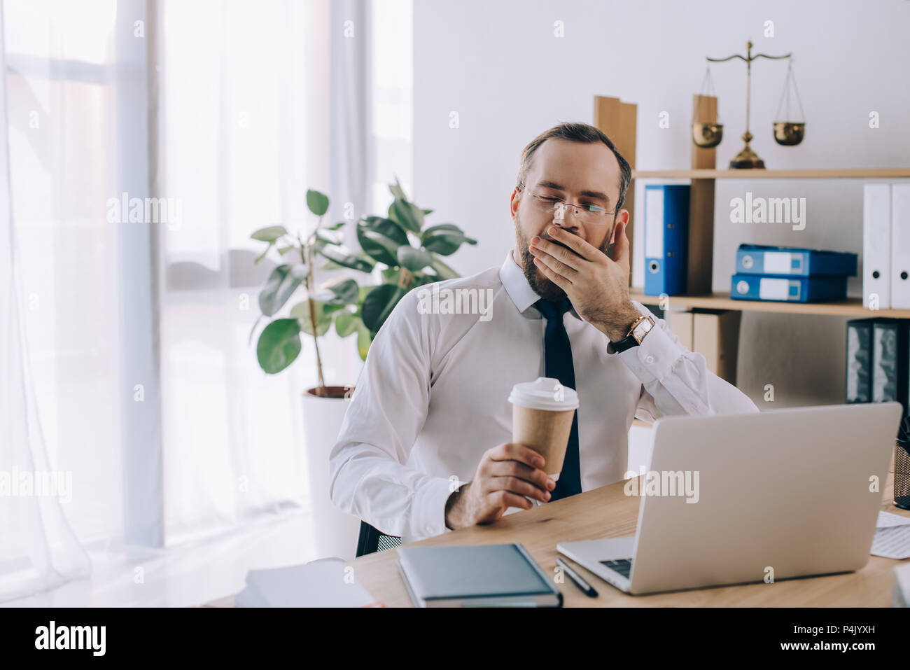 portrait of tired lawyer with coffee to go yawning at workplace in ...