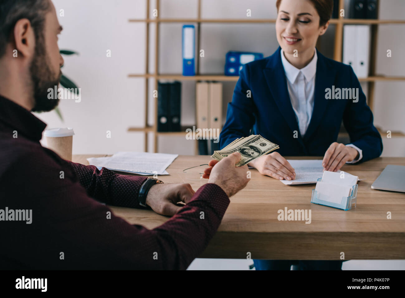 partial view of man giving bribe to smiling businesswoman at workplace ...