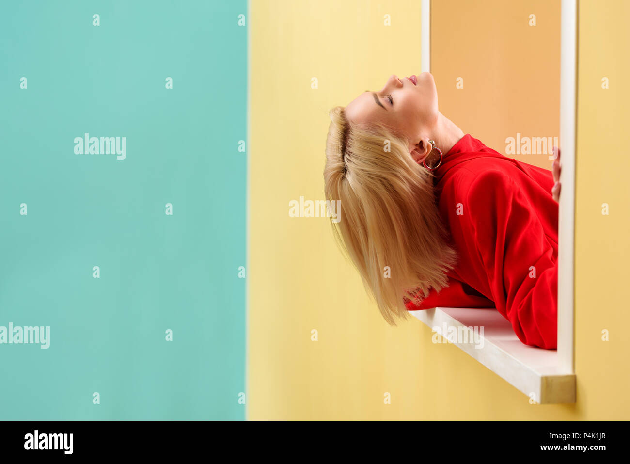 side view of attractive blond woman in red jacket at decorative window ...