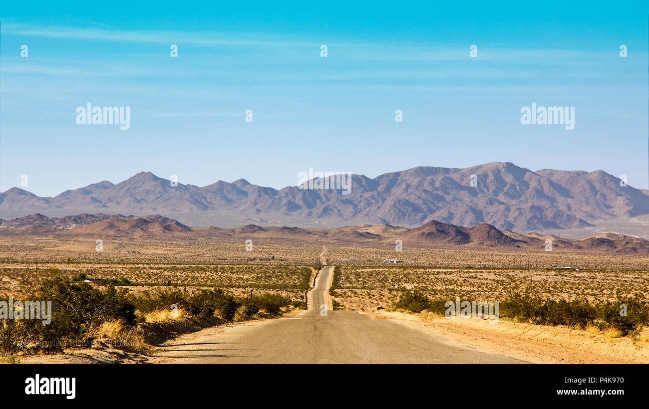 Long, straight and lonely desert road toward distant mountains, high desert landscape, mojave ...