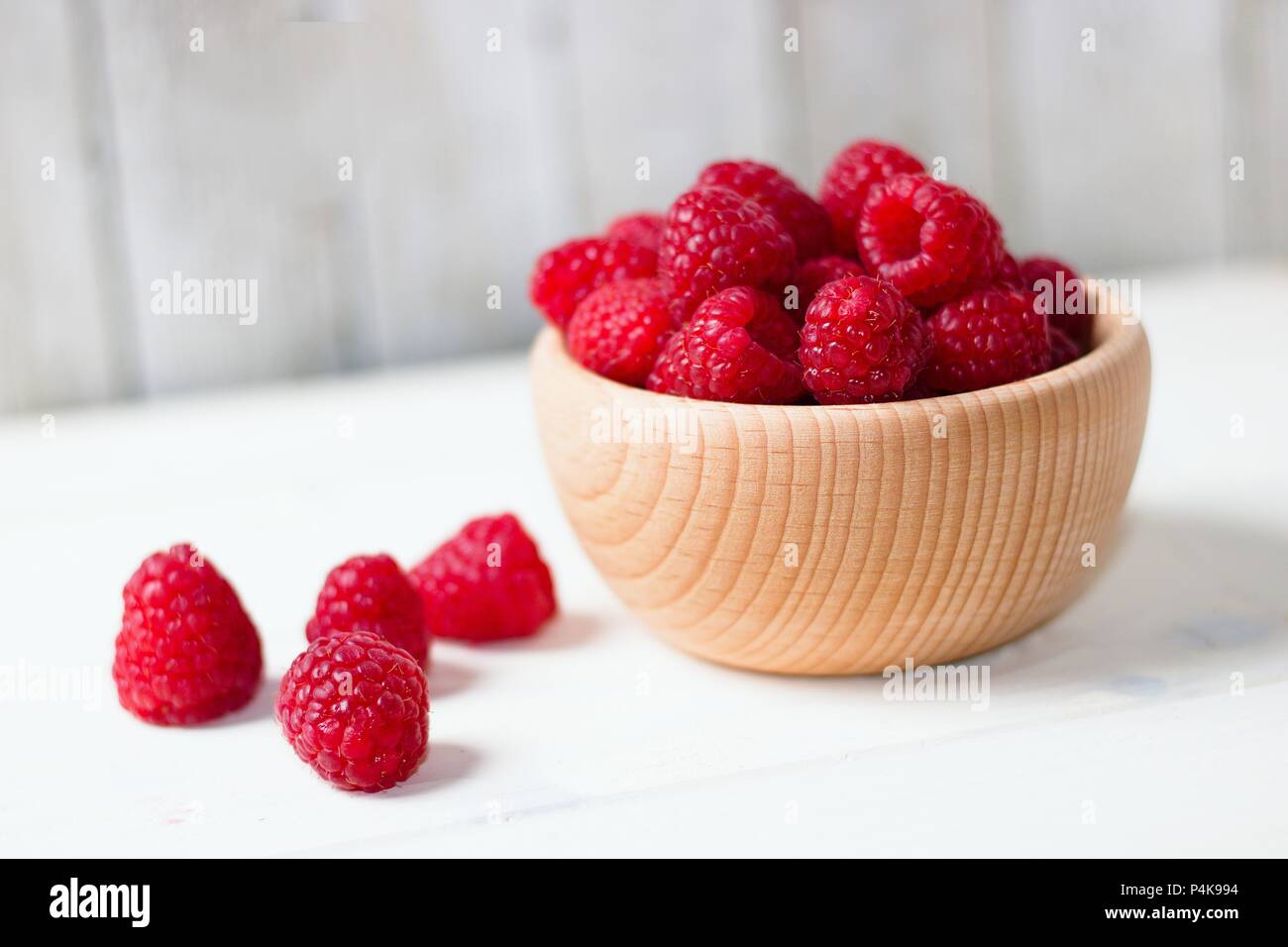 Wooden bowl full of raspberries set on white garden table with board ...