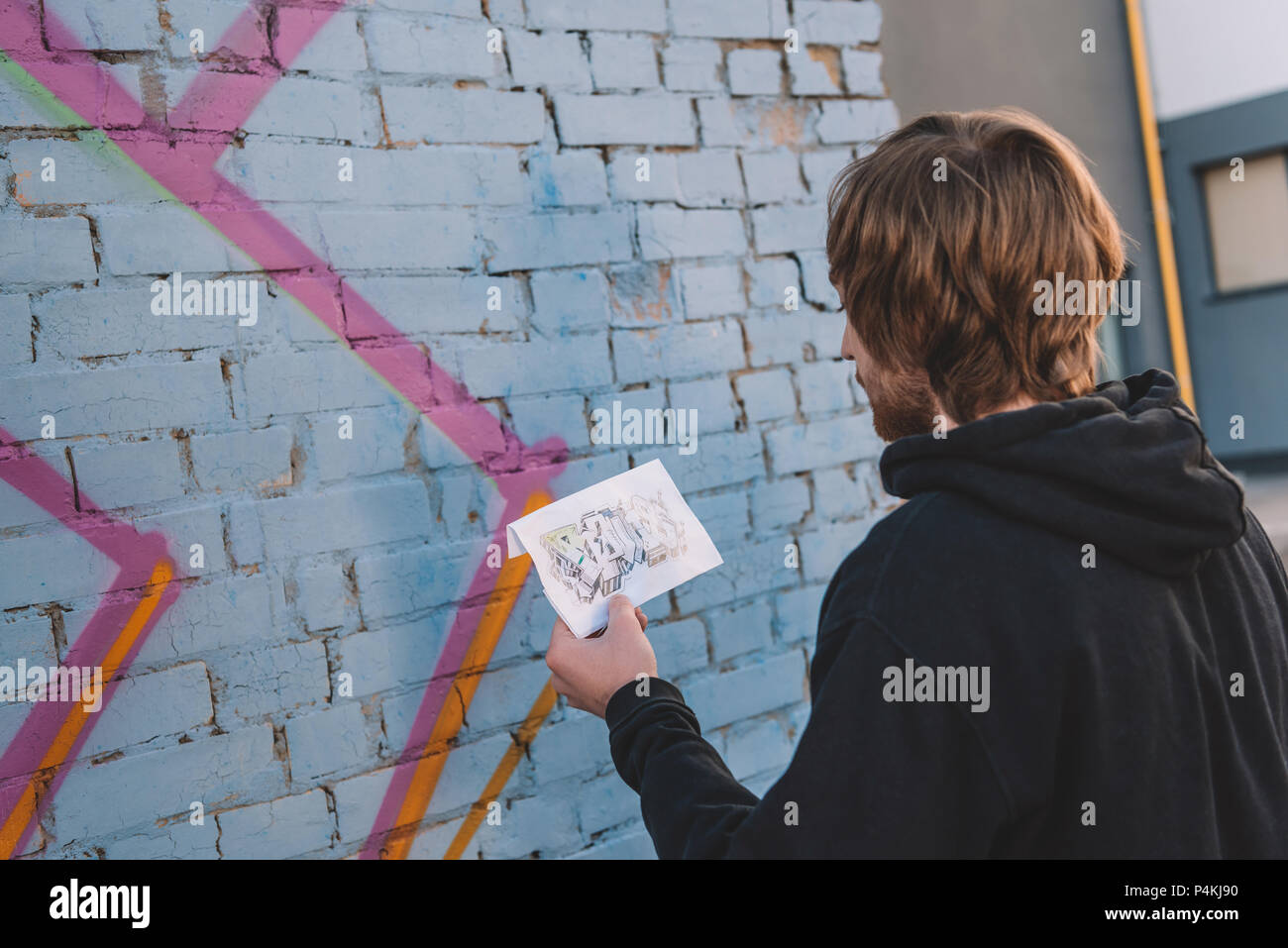 street artist looking at sketch and painting colorful graffiti on wall ...