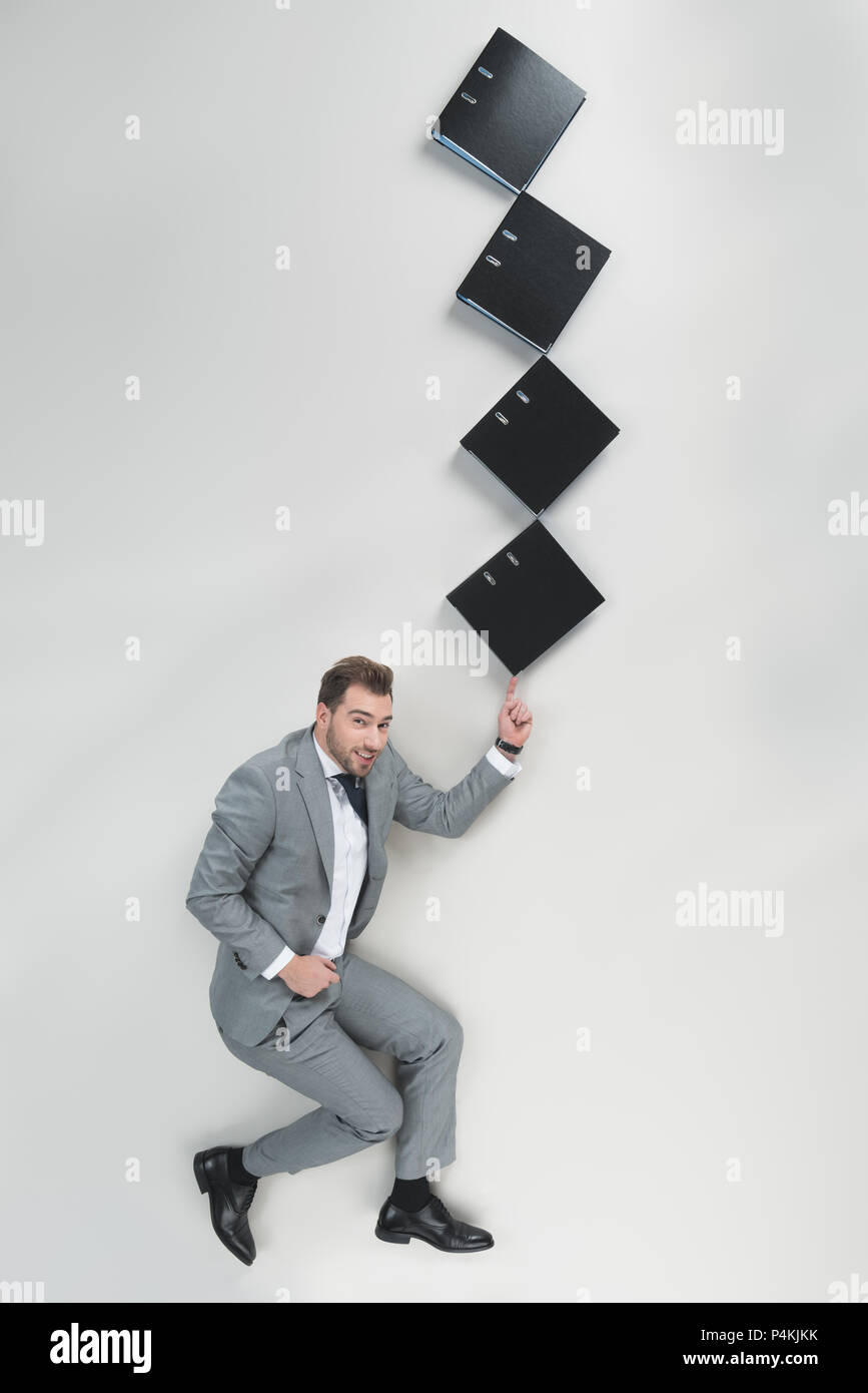overhead view of businessman holding stack of folders on one finger ...