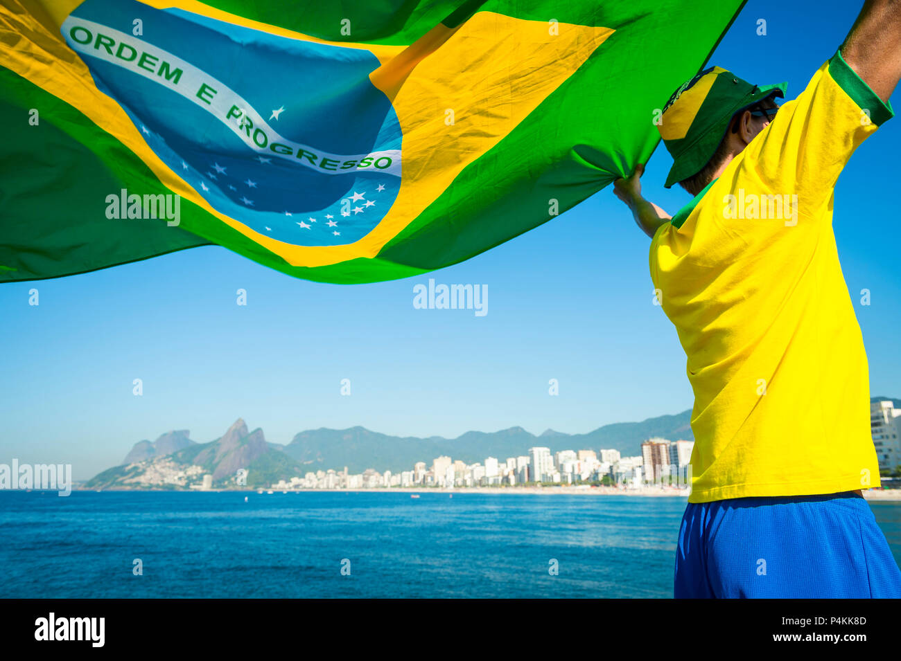 Brazilian football fan flying flag in front of Ipanema Beach city ...