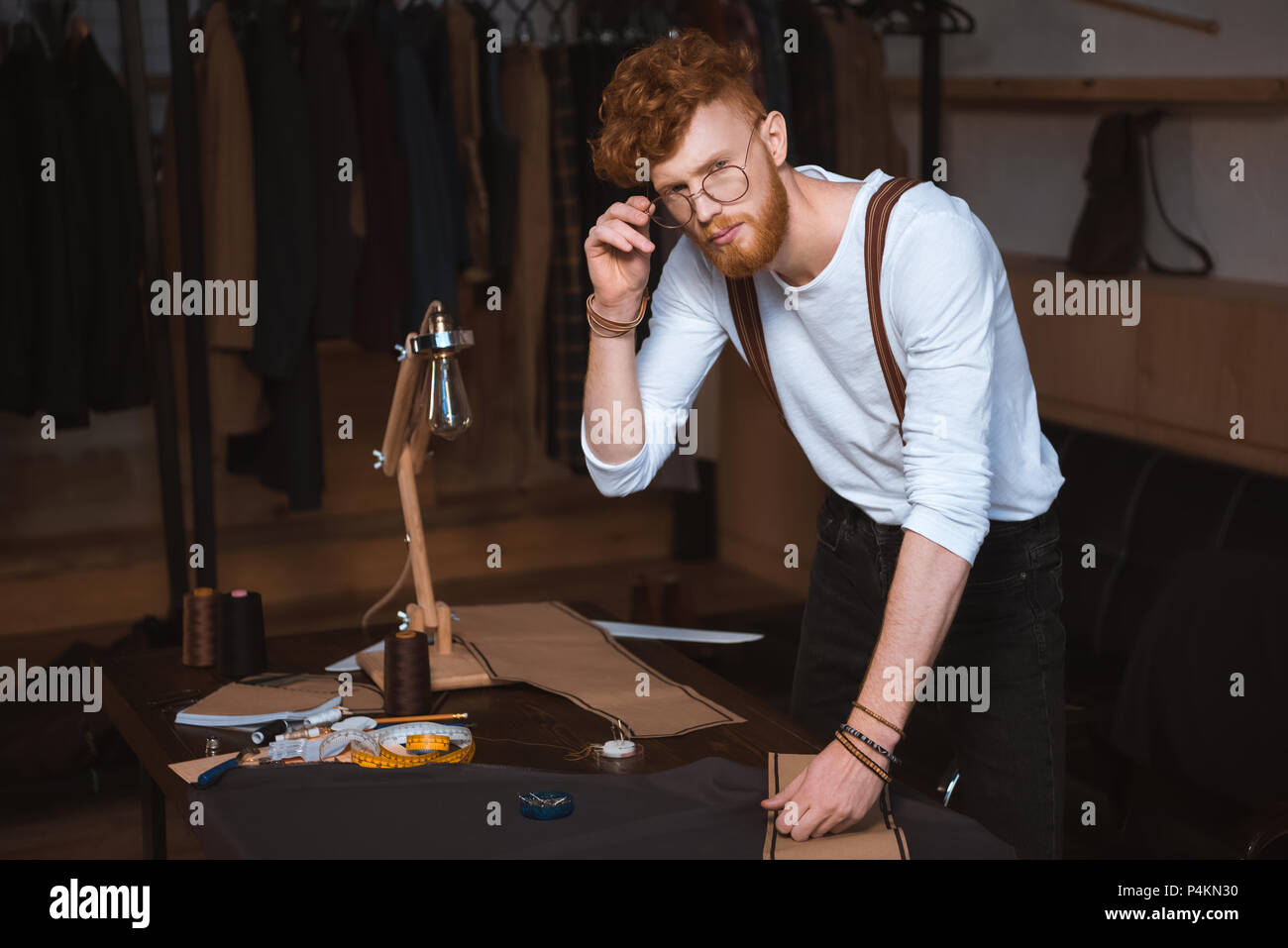 young male fashion designer in eyeglasses looking at camera while ...