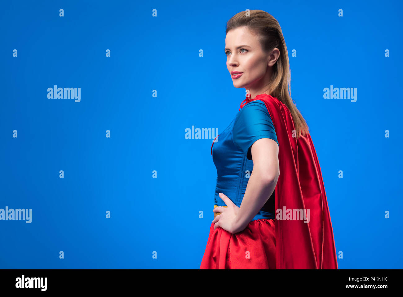 side view of beautiful woman in superhero costume standing akimbo ...