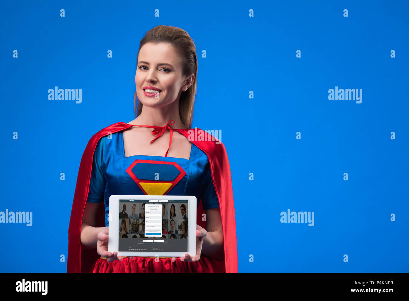 portrait of cheerful woman in superhero costume showing tablet isolated ...