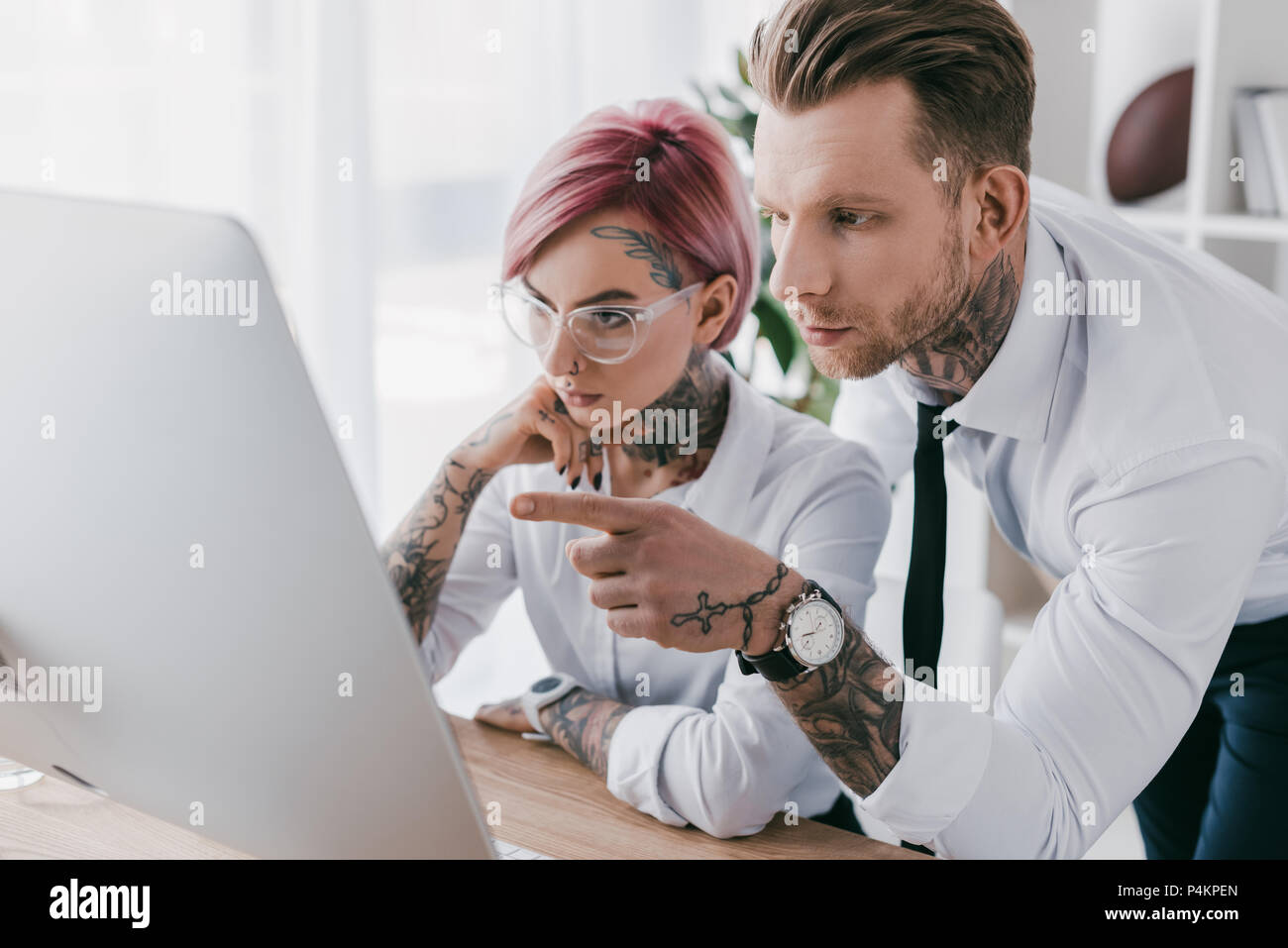 young tattooed business people in formal wear working with desktop ...
