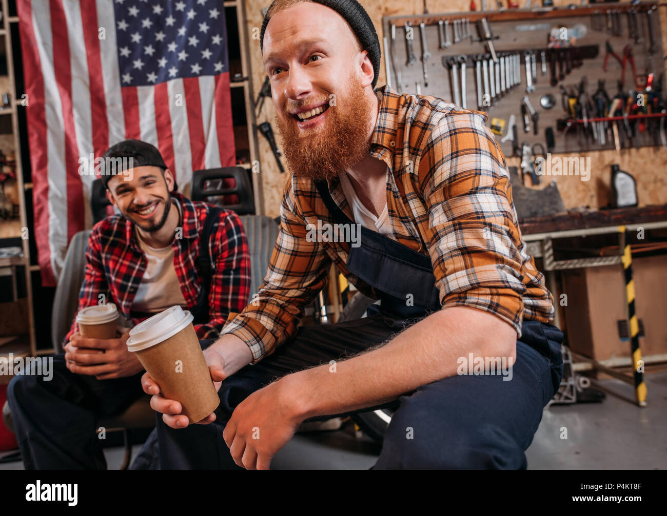 happy mechanics drinking coffee from disposable cups on break at garage ...