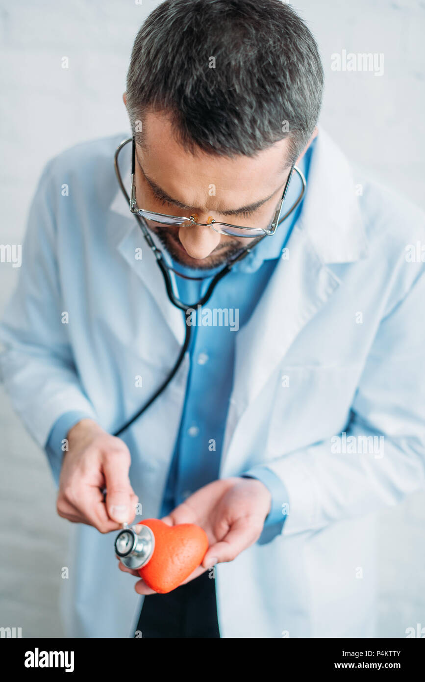 high angle view of doctor listening heartbeat of toy heart with ...