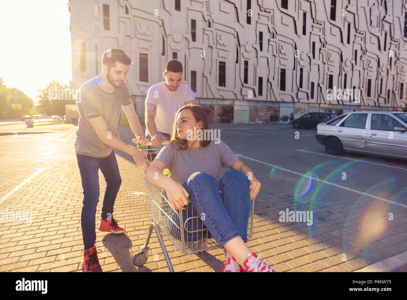 Teenage girl in shopping trolley having fun while two guys is pushing ...
