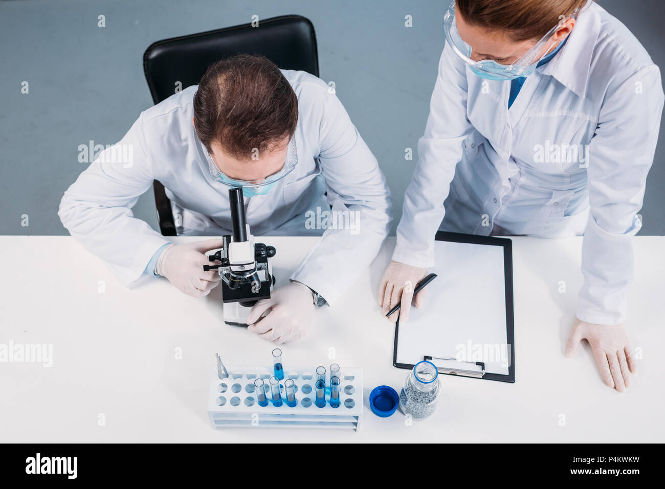 overhead view of scientists in medical masks and goggles working on ...