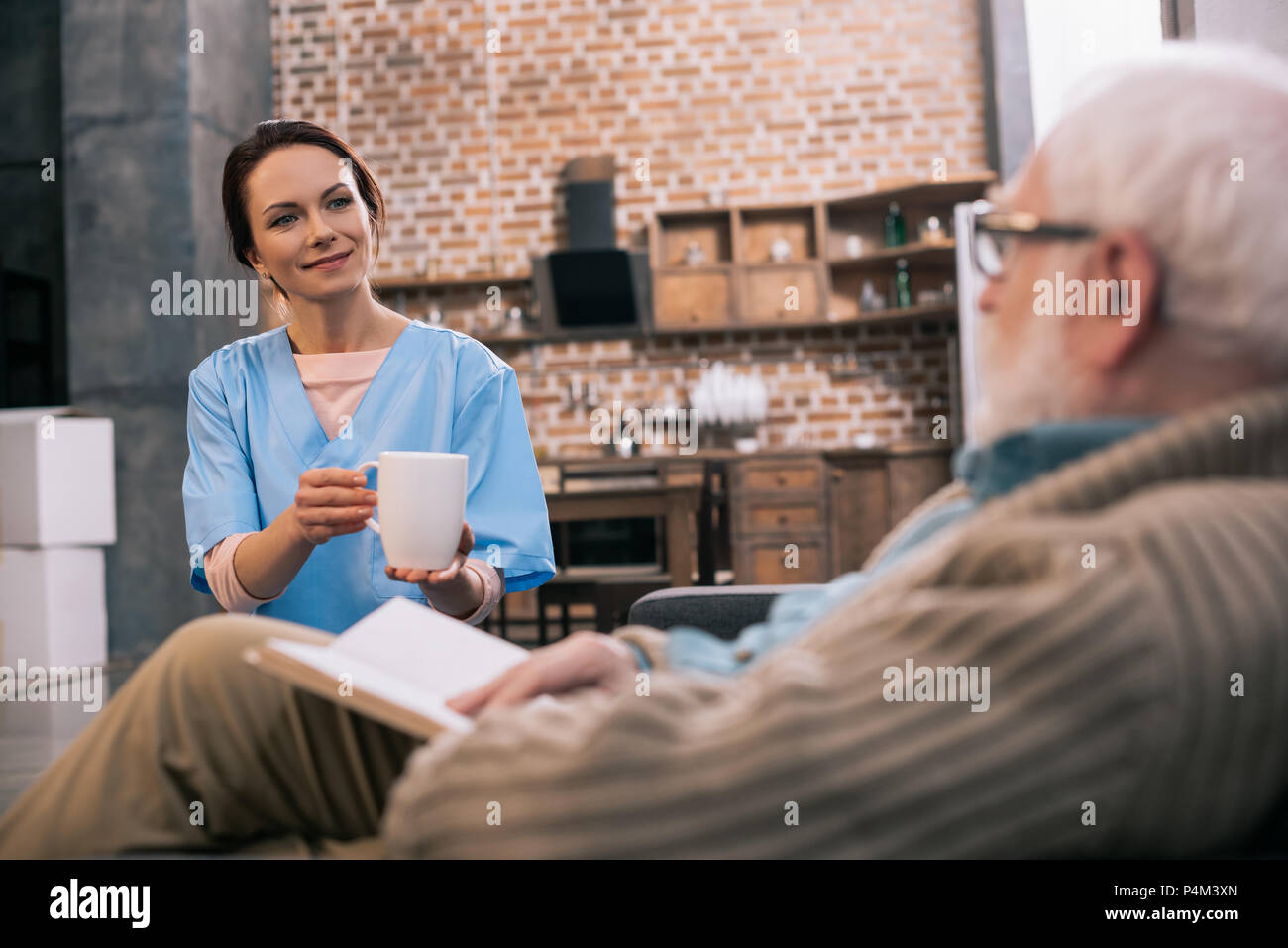 Nurse giving cup with drink to senior patient with book Stock Photo - Alamy