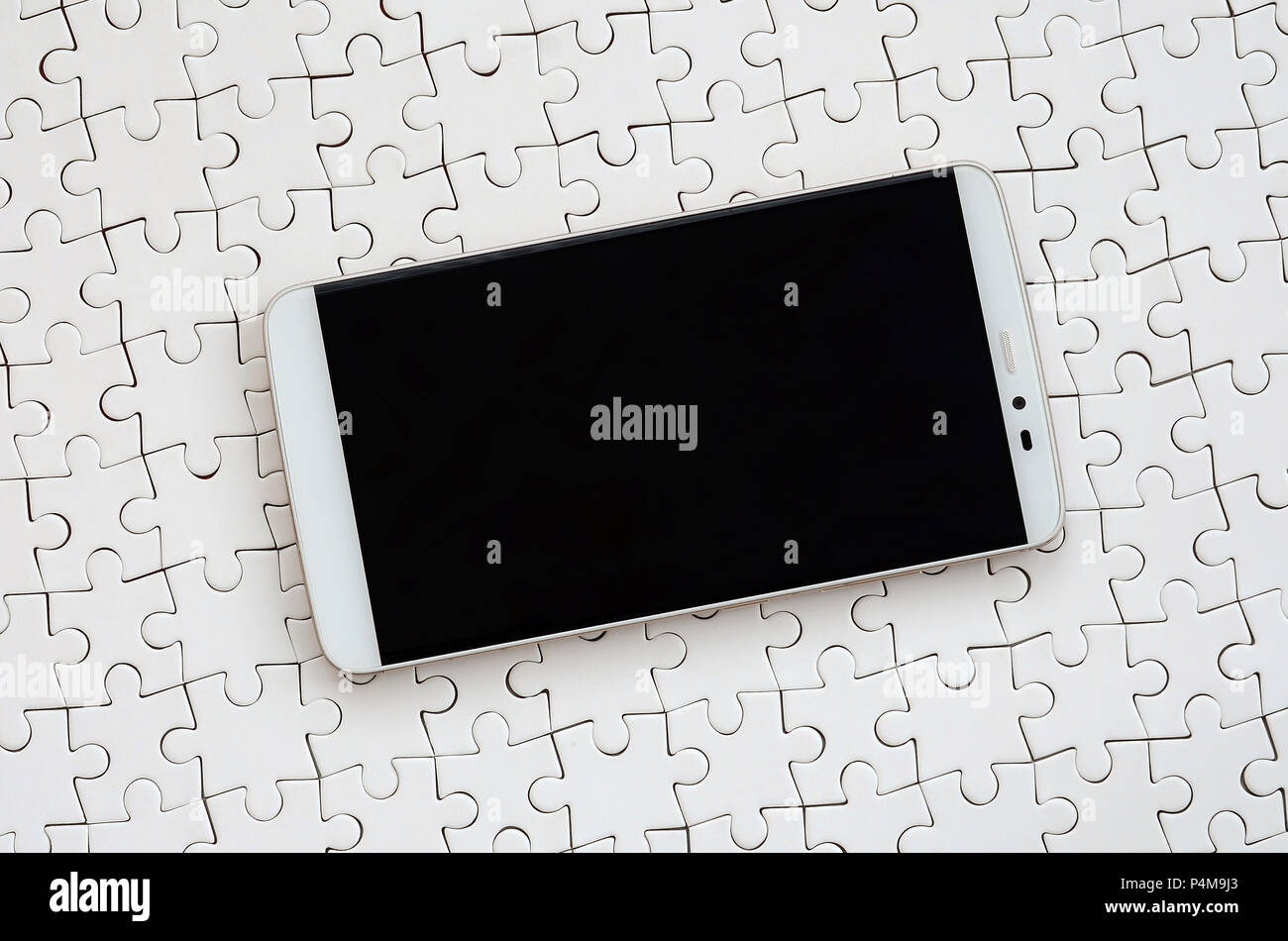 A modern big smartphone with a touch screen lies on a white jigsaw ...