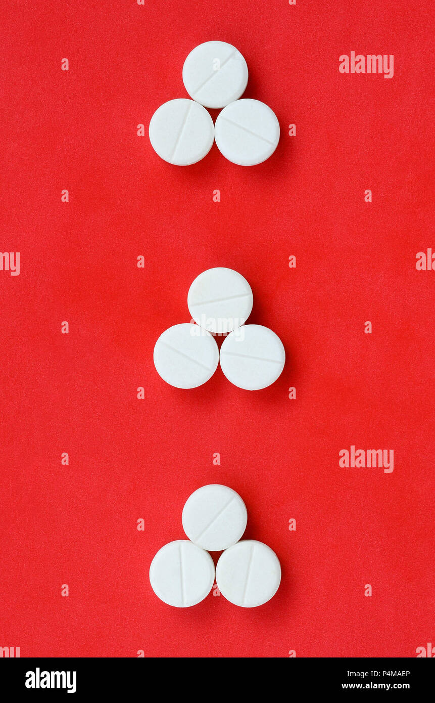Several white tablets lie on a bright red background in the form of ...
