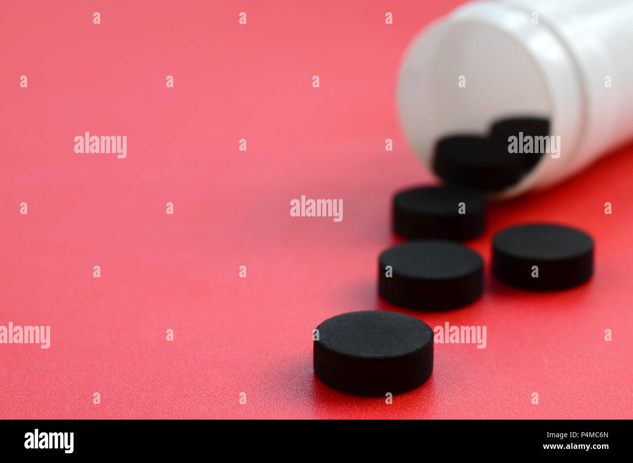 Several black tablets fall out of the plastic jar on the red surface ...