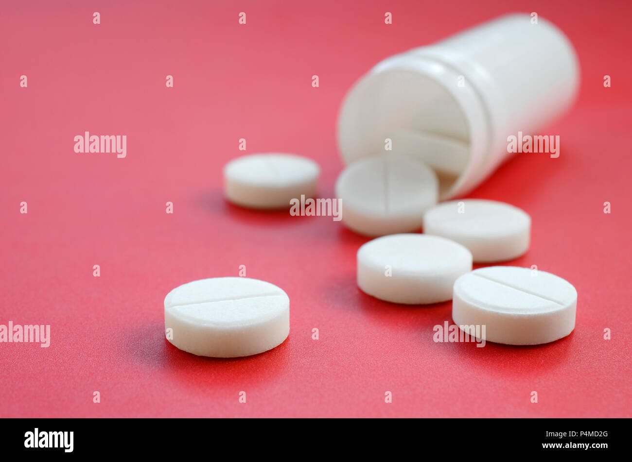 Several white tablets fall out of the plastic jar on the red surface ...
