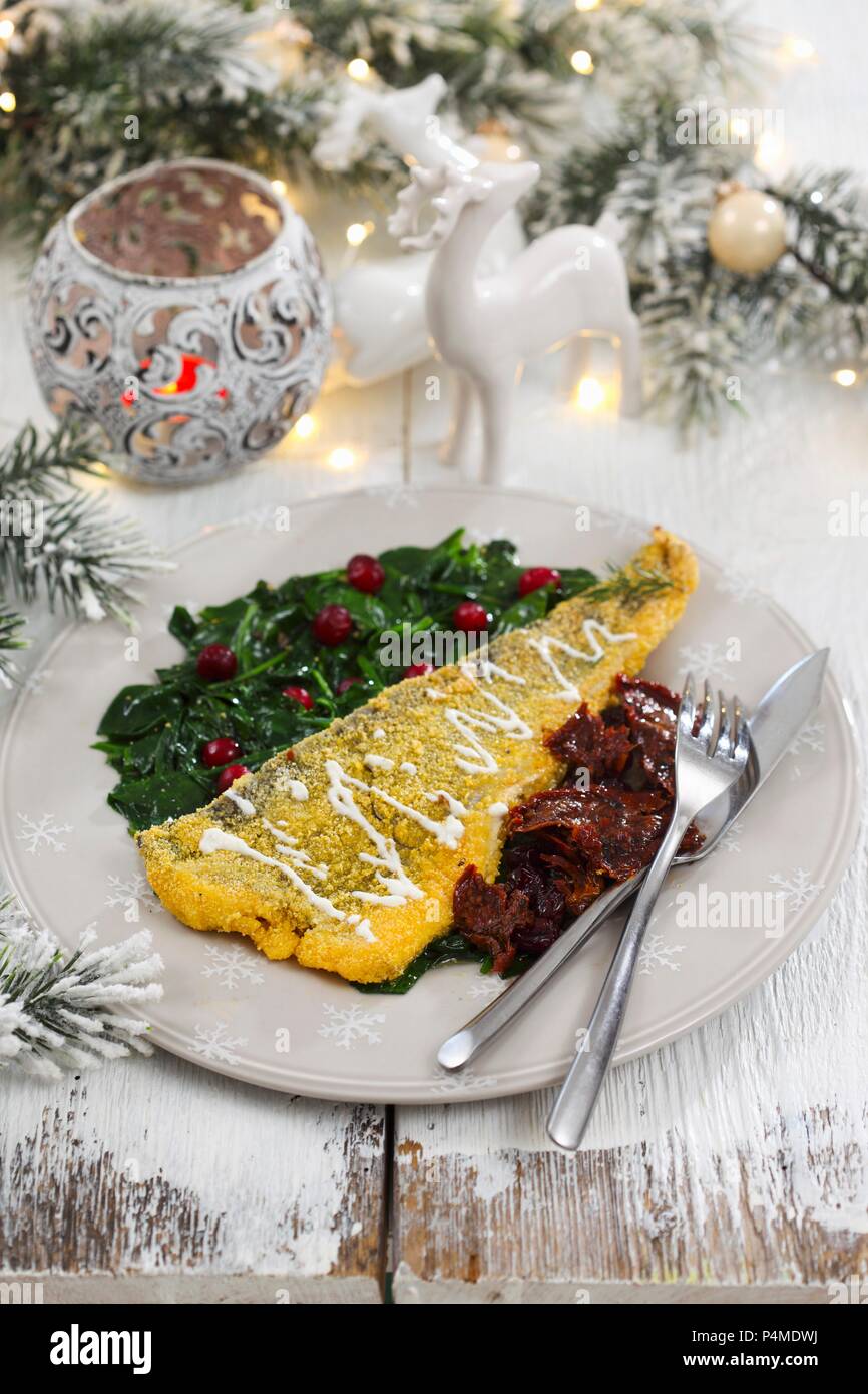 Fish fillet in polenta with spinach and dried tomatoes Stock Photo - Alamy