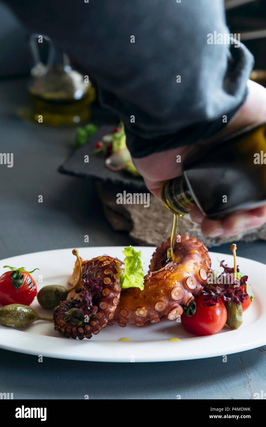 Olive oil being poured on octopus with tomatoes and giant capers Stock ...