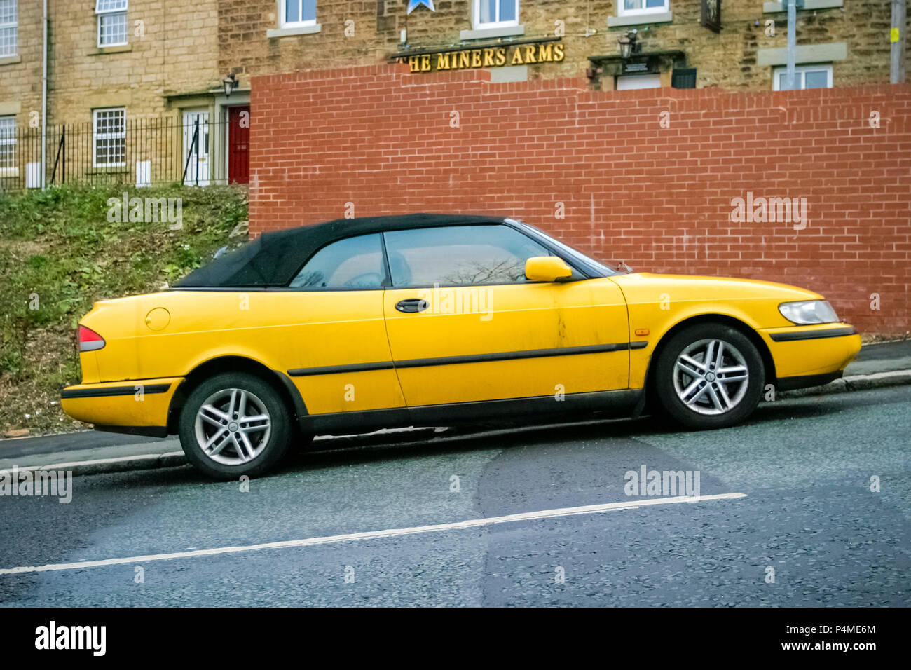 A yellow SAAB 900 convertible parked on a hill by the side of the road ...