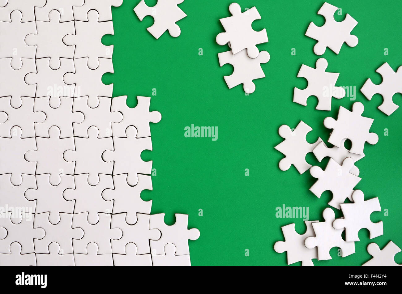Fragment of a folded white jigsaw puzzle and a pile of uncombed puzzle ...