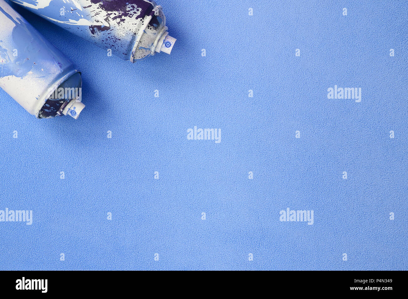 Some used blue aerosol spray cans with paint drips lies on a blanket of ...