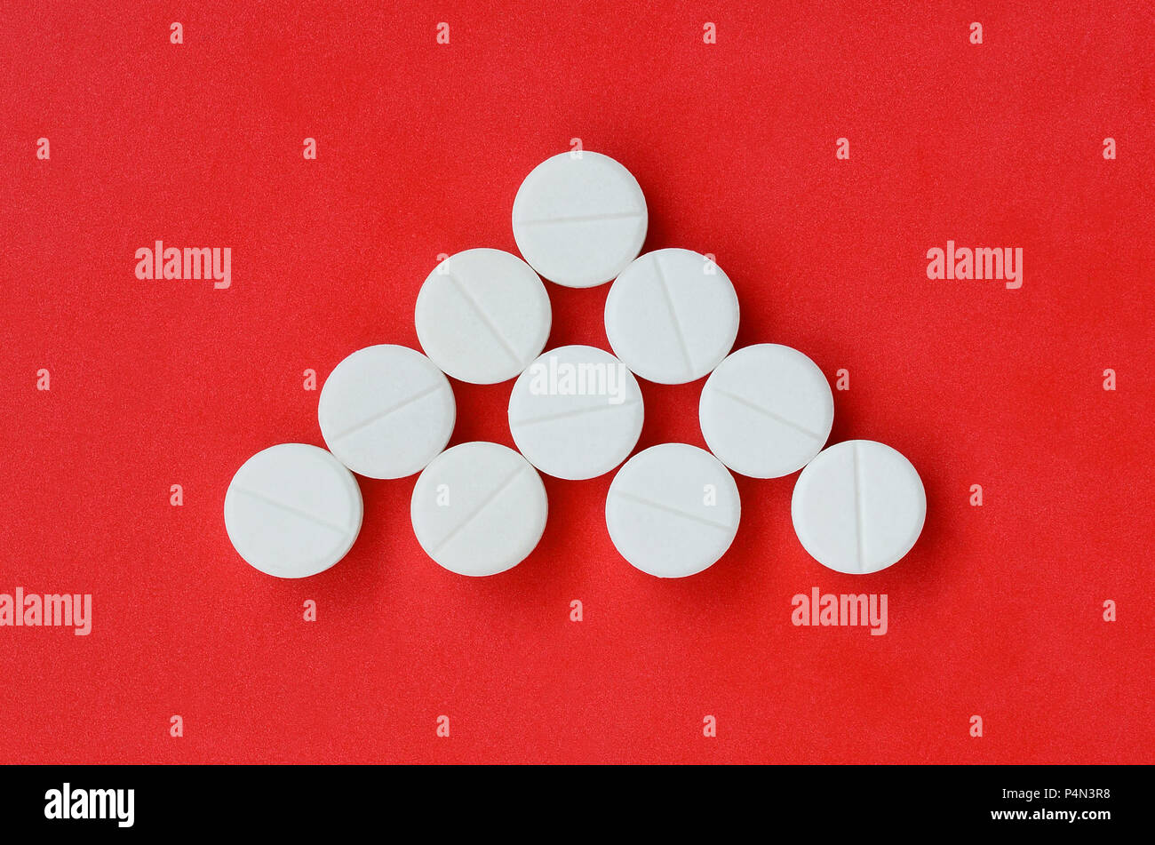 Several white tablets lie on a bright red background in the form of a ...