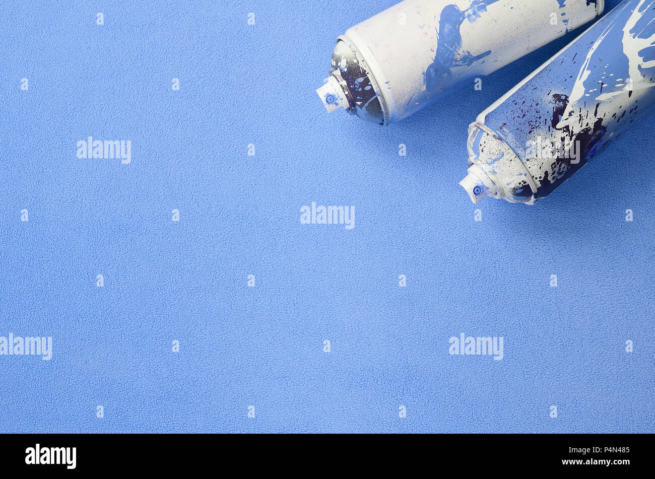 Some used blue aerosol spray cans with paint drips lies on a blanket of ...
