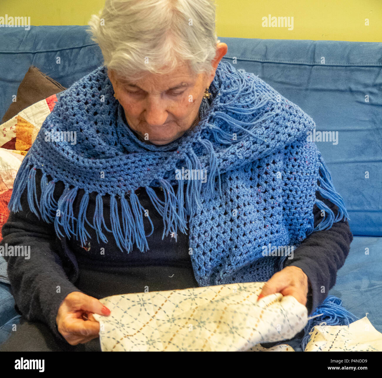 An elderly woman with white hair and wearing a shawl doing needlework ...