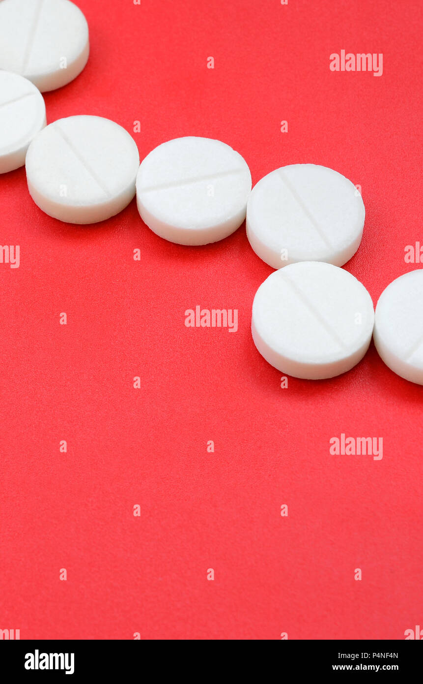 A few white tablets lie on a bright red background surface. Background ...