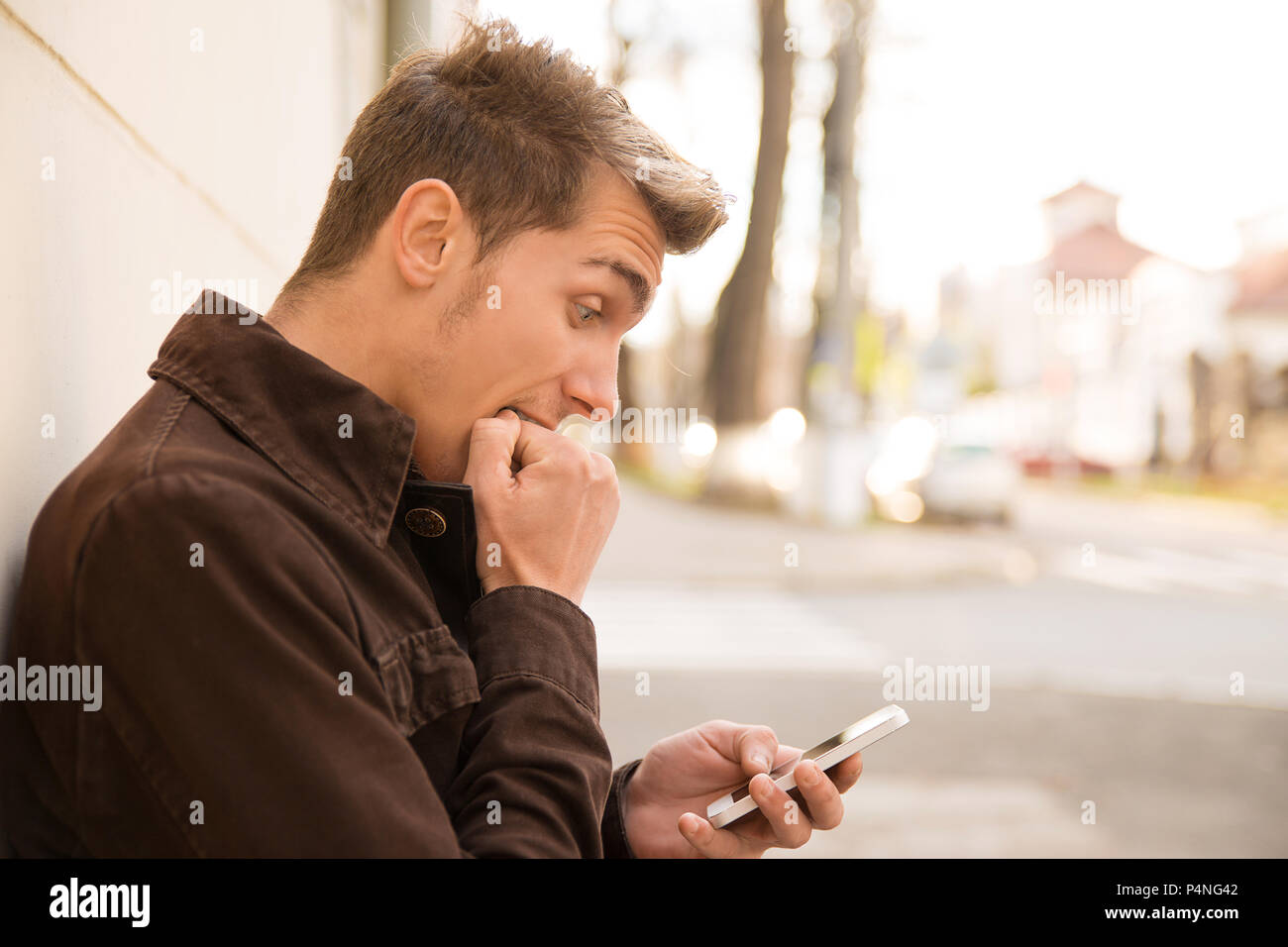 Side view of nervous scared man biting fist while looking at smartphone ...