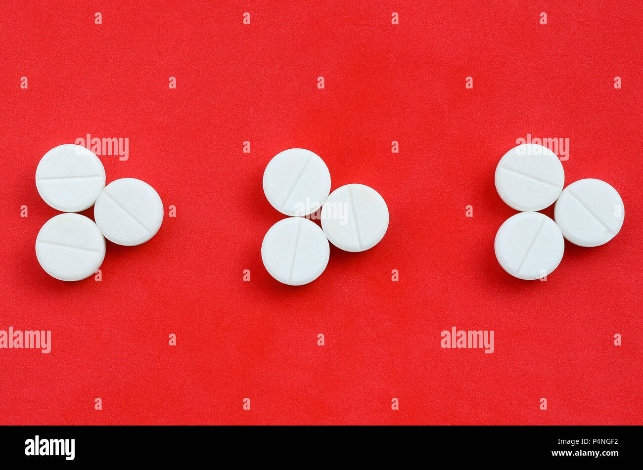 Several white tablets lie on a bright red background in the form of ...