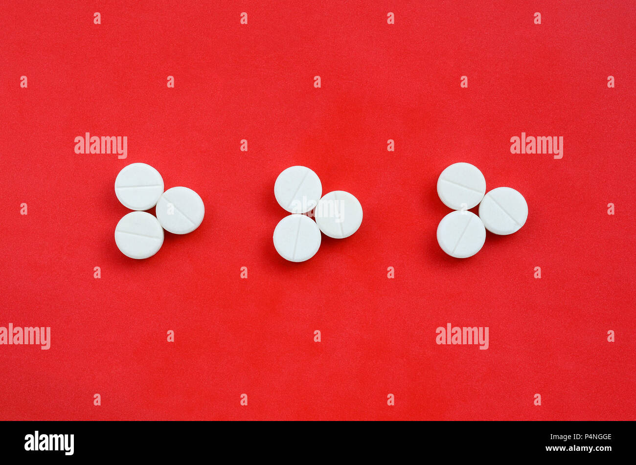Several white tablets lie on a bright red background in the form of ...