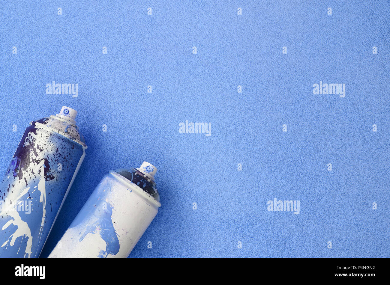 Some used blue aerosol spray cans with paint drips lies on a blanket of ...