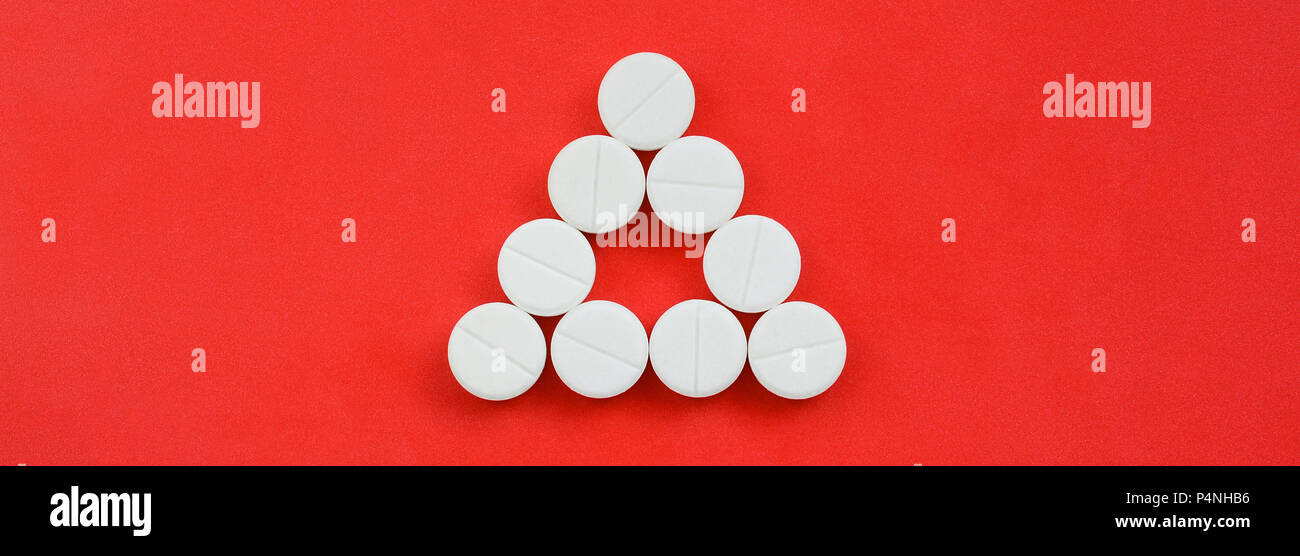 Several white tablets lie on a bright red background in the form of an ...