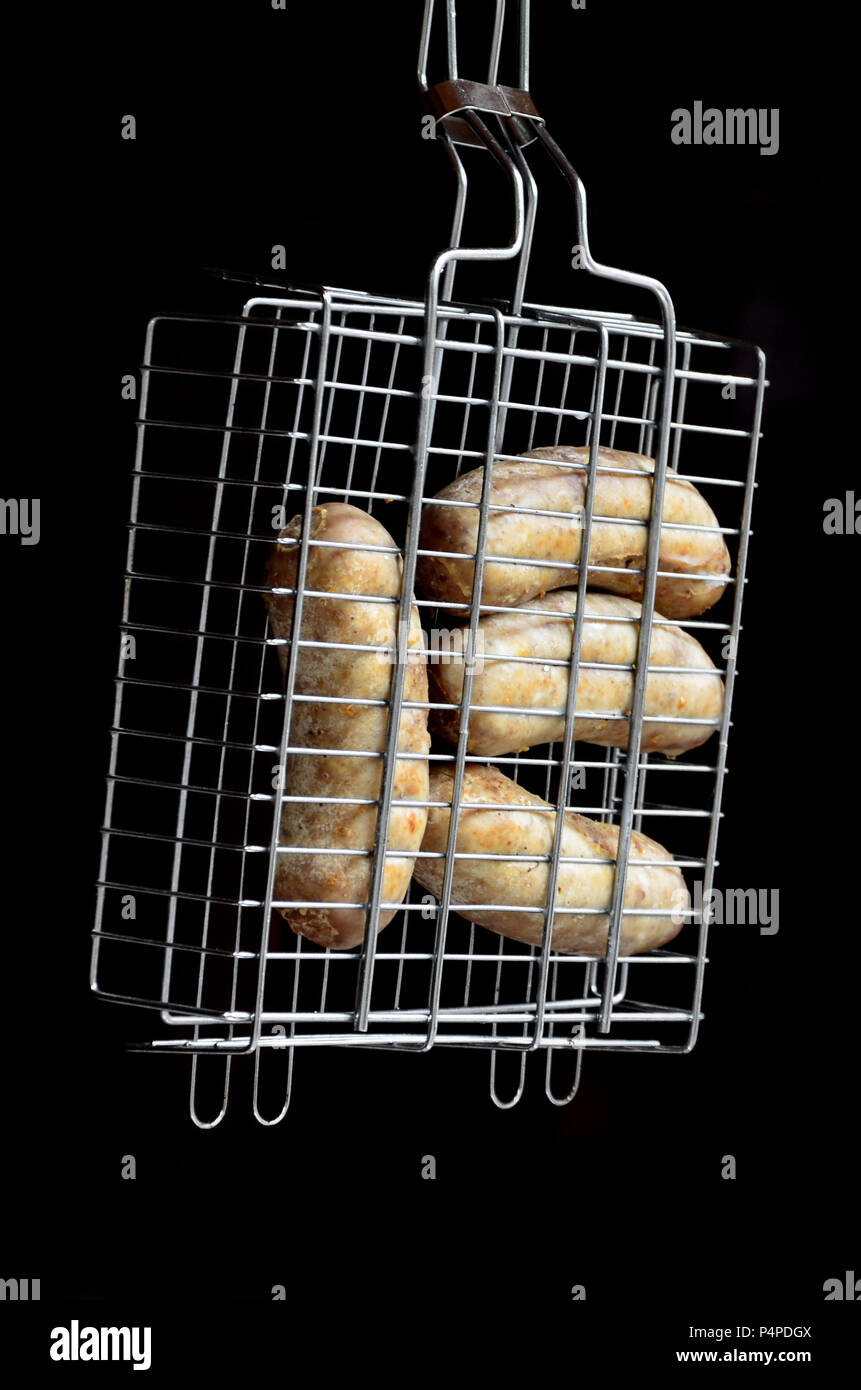 A small hand grill is filled with fried thick sausages on a dark ...