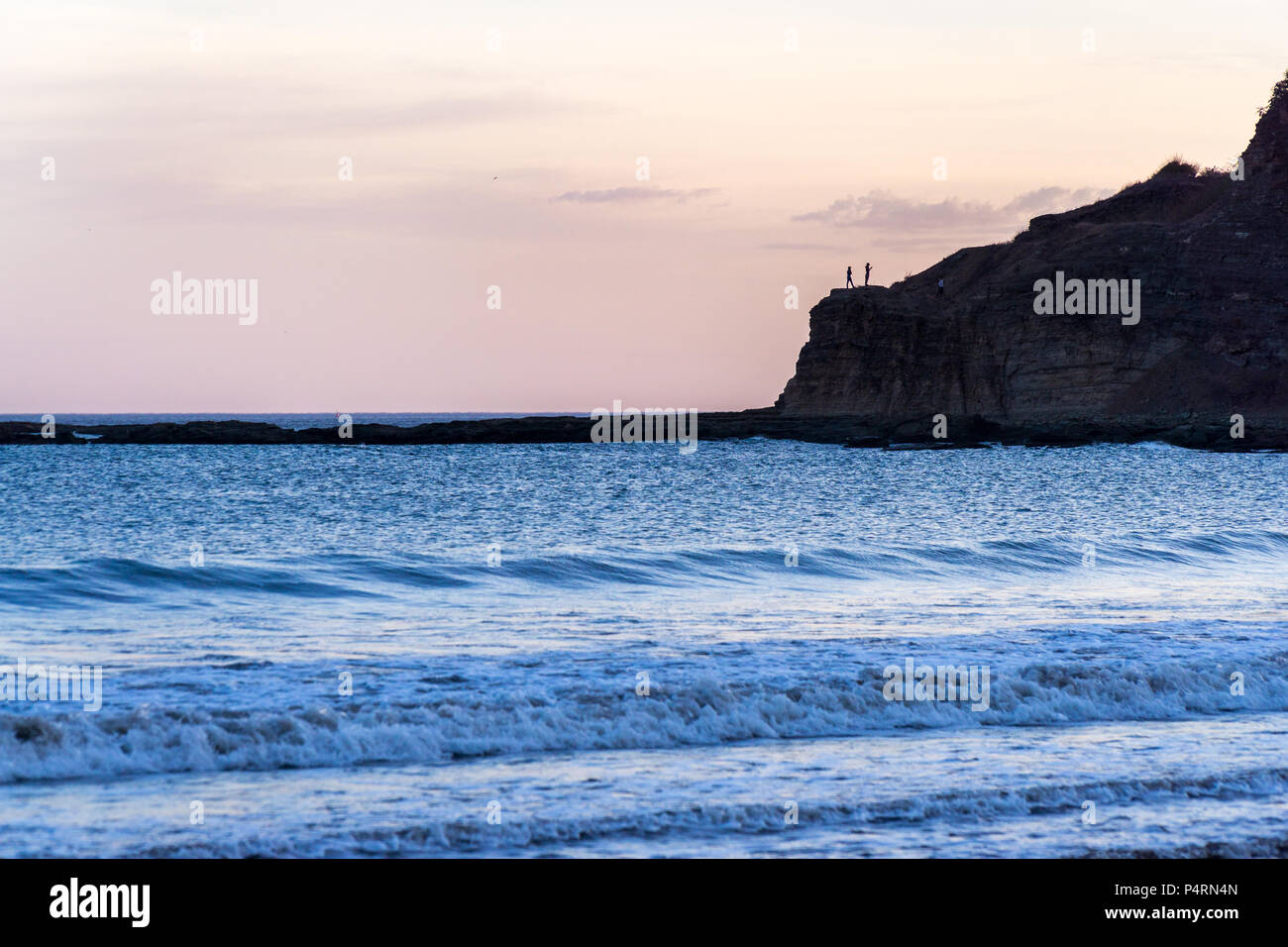 Silhouette of two persons standing on a rock at the beach in the ...